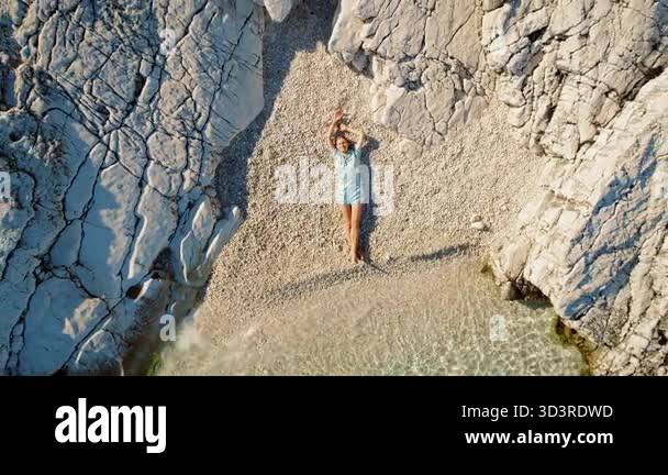 Woman lying on pebbled beach cove between rocks by crystal clear sea ...