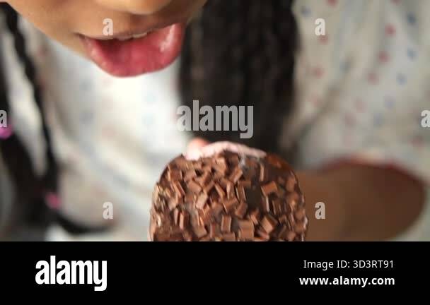A child joyfully takes a big bite of chocolate ice cream topped with ...