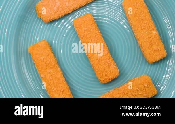 Frozen breaded cod fish fingers rotating on a blue plate. Ready-to-cook ...