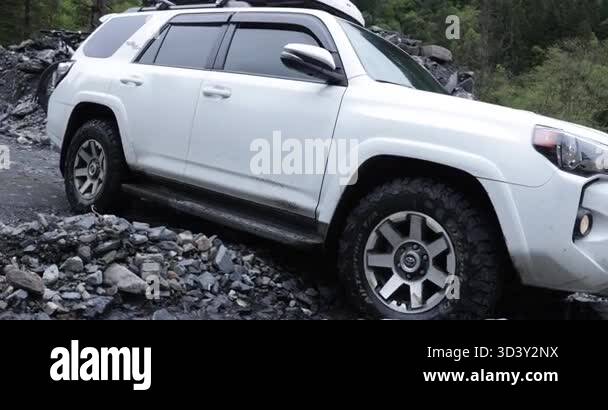 A white SUV driving off-road over a bed of rough, dark rocks and gravel ...