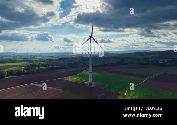A tall wind turbine stands proudly on rolling farmland as clouds drift ...