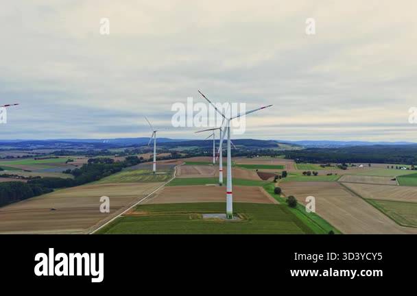 Tall wind turbines rotate slowly atop rolling green hills set against a ...