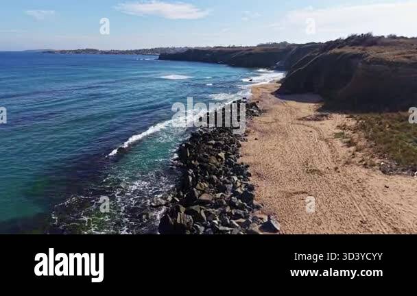 At a quiet beach, sunlit rocks border the soft sand, where waves ...