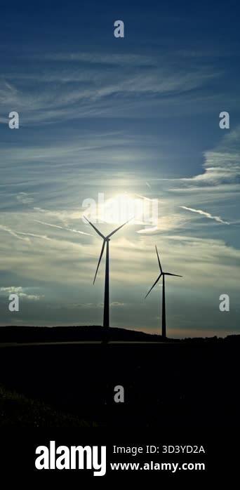 Tall wind turbines stand proudly silhouetted against the sky as the sun ...