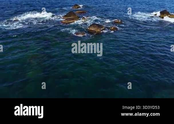 Waves softly lap against rocky formations jutting out of a clear ...