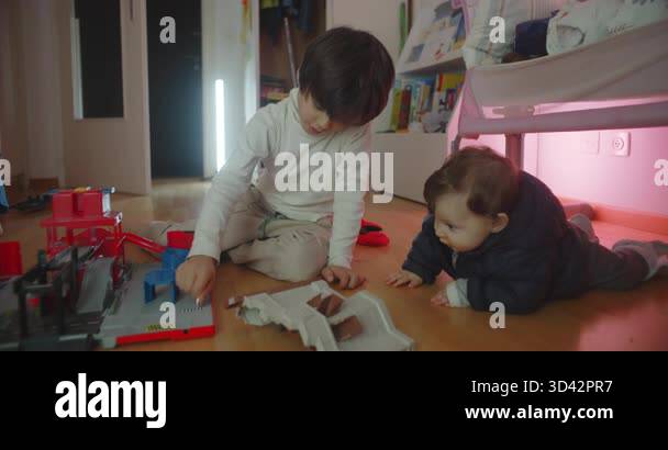 Older brother sitting on the floor showing his baby brother how to play ...