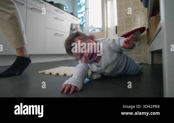 Baby lying on kitchen floor crying with leg stuck under cabinet shelf ...