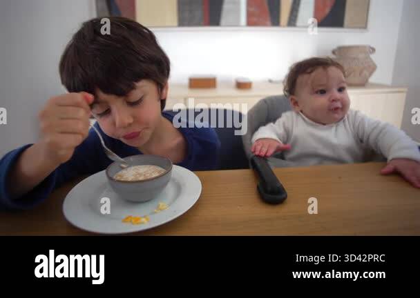 Older brother eating cereal beside baby sibling at breakfast sharing ...
