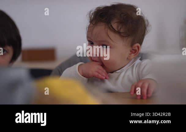 Baby sitting in chair with hand in mouth, expressing curiosity and ...