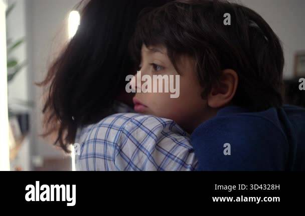 Boy leaning on mother's shoulder at breakfast table, looking away with ...