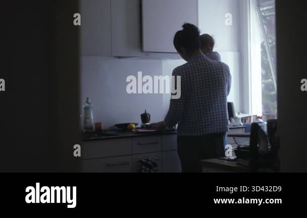 Mother cooking in kitchen while holding baby, multitasking between ...