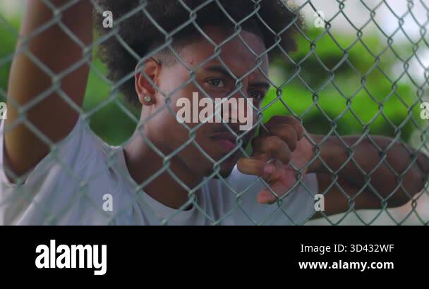 Young African American man behind fence looking upward with subtle hope ...