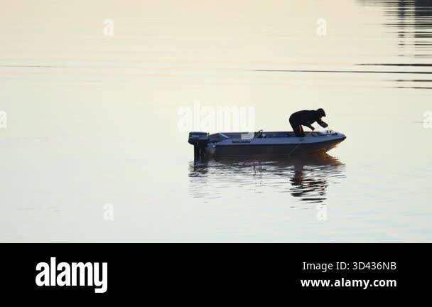Fisherman in a small boat catching fish at sunrise on calm sea ...
