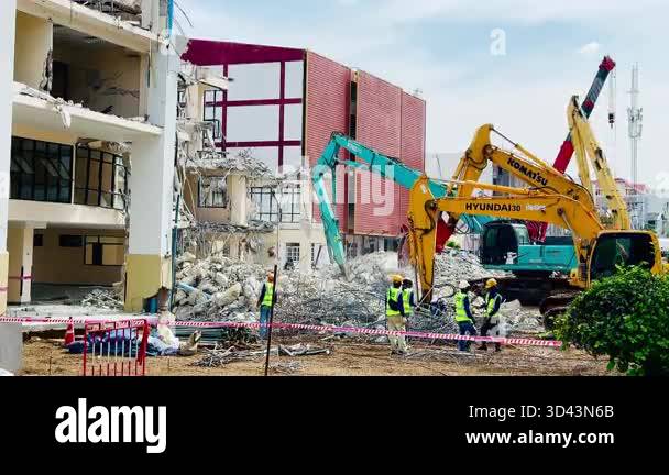 Workers and excavators demolish an old building at a construction site under clear sky. Safety ...