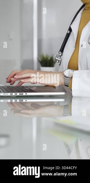 Female doctor working on laptop, managing patient data, writing ...