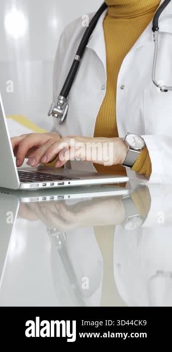Female doctor working on laptop, managing patient data, writing ...