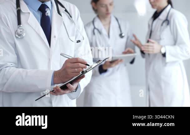 Healthcare worker in a lab coat updating patient records on a clipboard ...