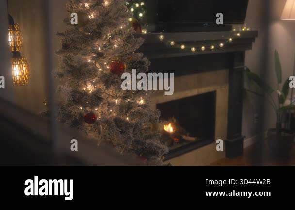 Fireplace burning next to a Christmas tree at home, while snow falling ...