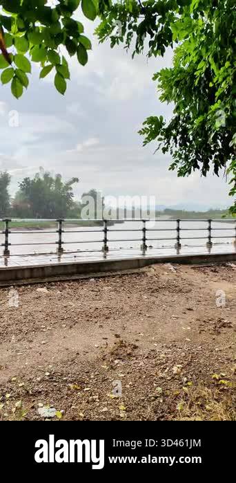 Heavy Rain Falling on River Embankment with Green Trees and Overcast ...