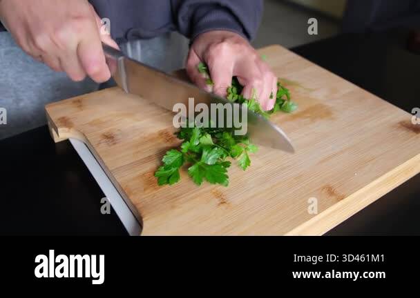 Close-up of hands chopping fresh parsley with knife on wooden cutting ...