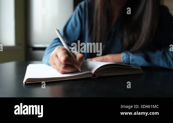 Close-up of a girl writing notes in a paper notebook at home, simple ...
