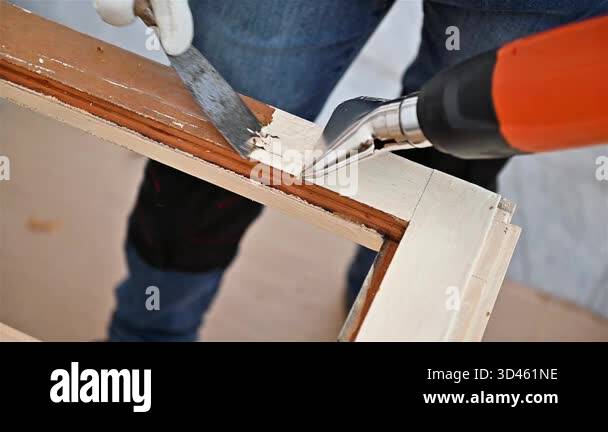 Carpenter using heat gun and wood scraper removes paint from old wooden ...
