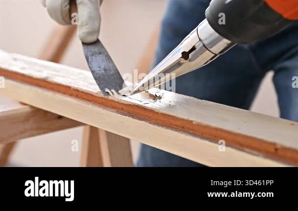Carpenter using heat gun and wood scraper removes paint from old wooden ...