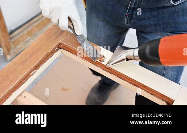 Carpenter using heat gun and wood scraper removes paint from old wooden ...