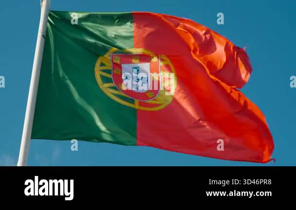 Slow motion close-up view of the flag of Portugal flying against a blue ...