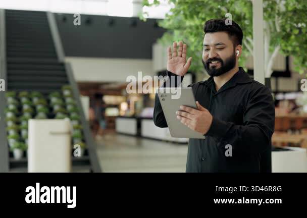 Portrait of friendly Indian salesman with earphones waves hand to ...