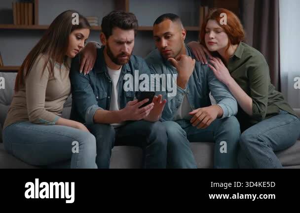 Surprised four multiracial friends at home party looking mobile phone ...