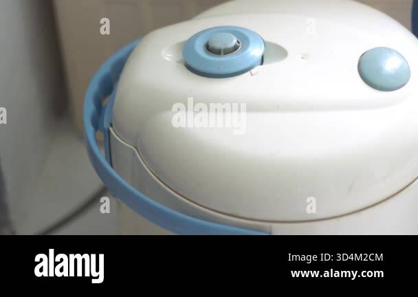 A person opens a rice cooker lid while hot steam rises and water drips ...