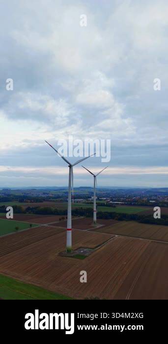 Two tall wind turbines stand proudly in farmland, their blades turning ...