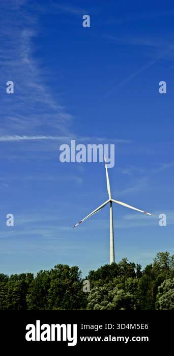 A large wind turbine spins against a blue sky. Green energy production ...
