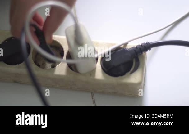 A person plugging an electrical device into a messy power outlet with ...