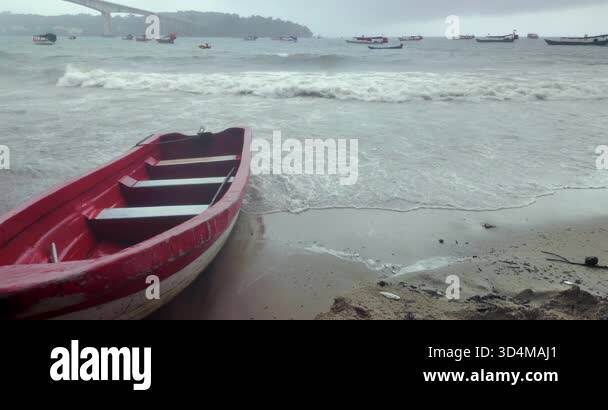 Choppy waves wash ashore past a beached red boat, while a fleet of ...