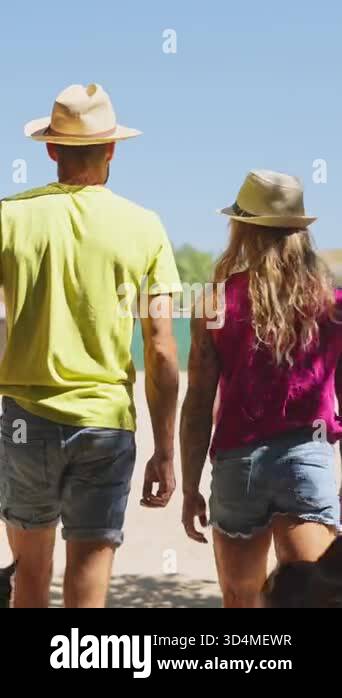 Back view of a man and a woman with hats holding hands while walking ...