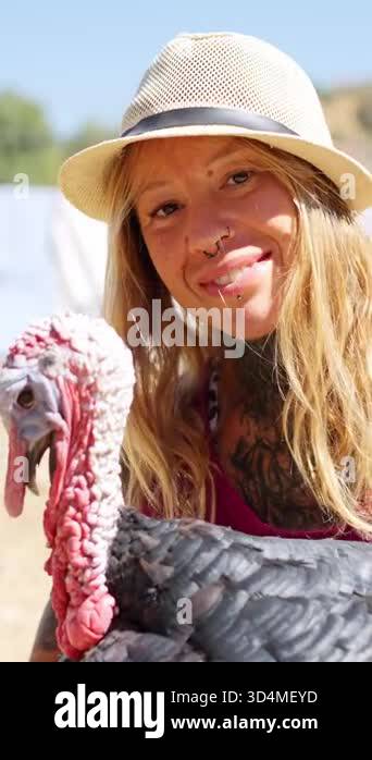Happy tattooed woman smiling and cuddling a large turkey on a sunny day ...