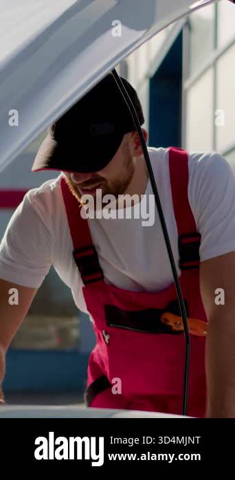 Male mechanic in red overalls is focused on car engine, using ...