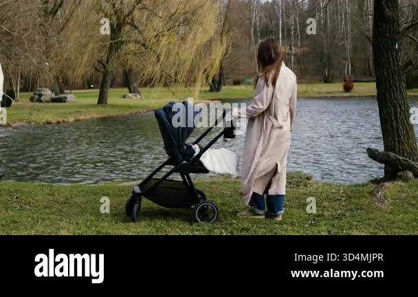Female figure in light coat interacts with stroller near calm water ...