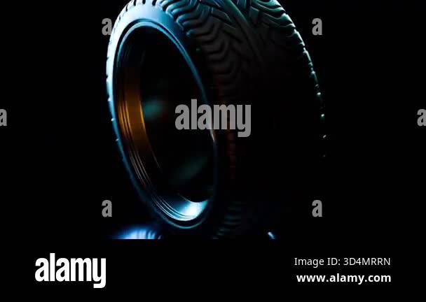 A single tyre with alloy rim rotates in place on a cool blue studio ...