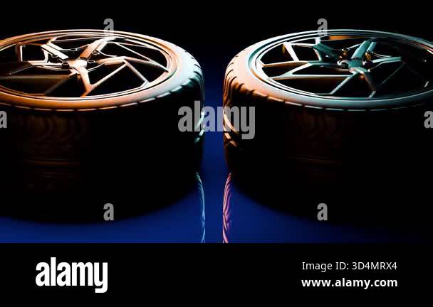 Two tyres with alloy rims rotate together on a dark studio stage ...