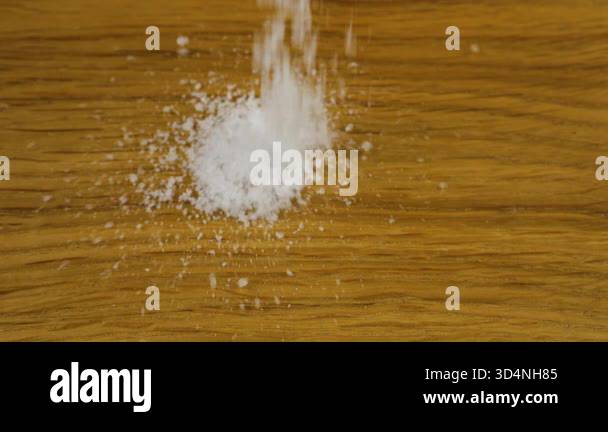 Fine crystals of natural sea salt fall onto a wooden surface. A big ...