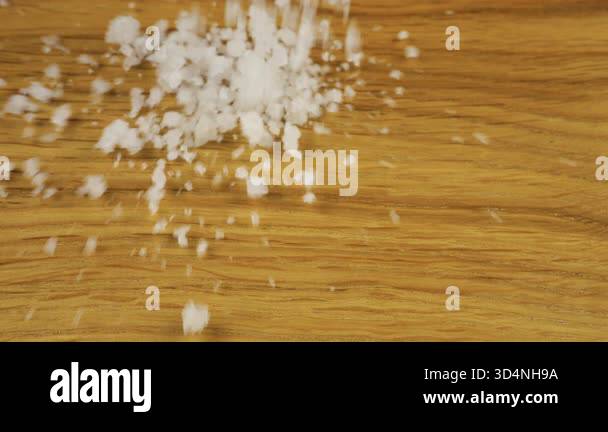 Large crystals of natural sea salt fall onto a wooden surface. A big ...