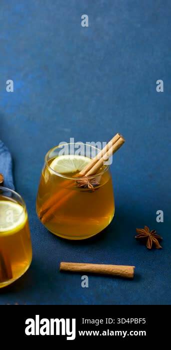 Warm beverage in glass with lemon, cinnamon sticks and star anise on ...