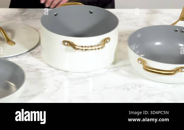 Two large white ceramic cooking pots with golden handles sit side by ...