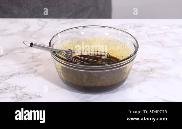 A whisk rests inside a glass bowl filled with a frothy liquid mixture ...