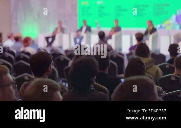 Conference scene with seated audience watching panel on stage under ...