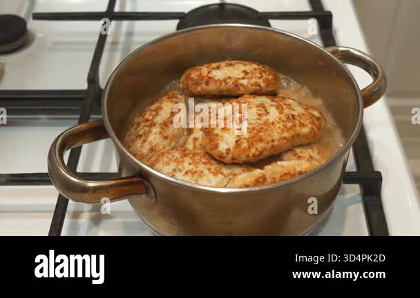 Meat cutlets are stewed in saucepan. Cook opens and closes the lid of ...