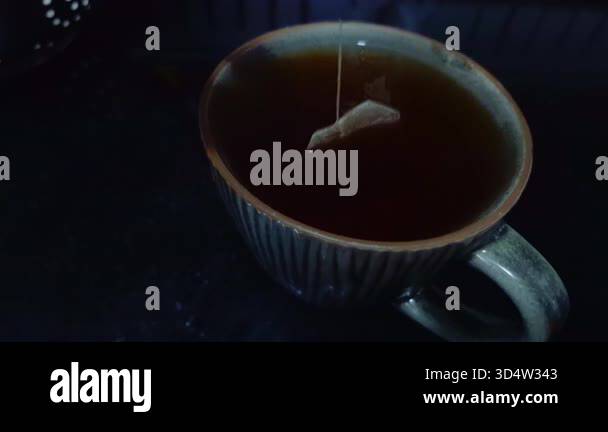 A tea bag is dipped into a cup of water to brew black tea, illustrating ...